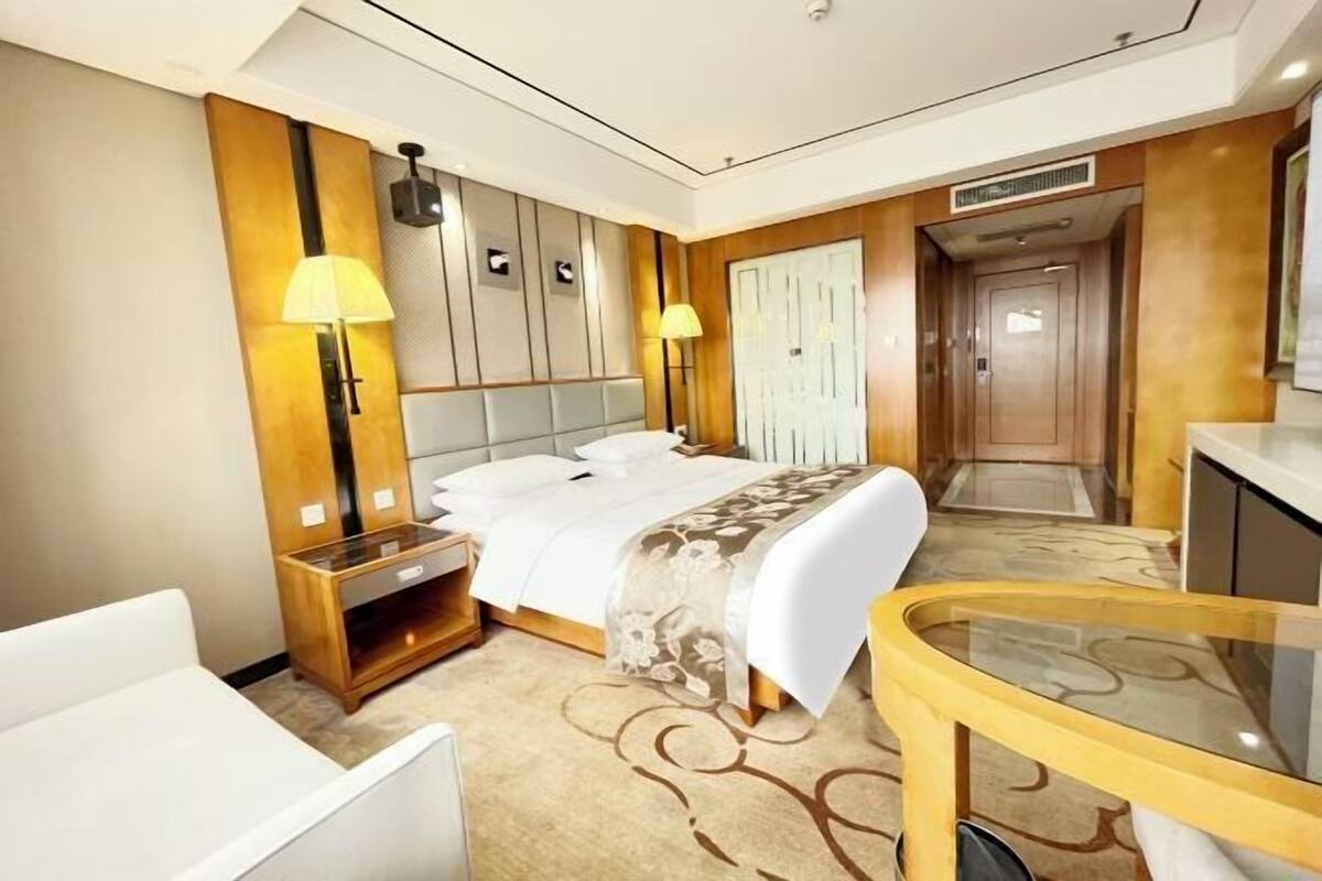 Quarto de hotel com cama, mesas de cabeceira, escrivaninha, cadeira e abajur.