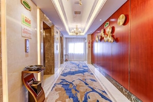 Corredor de hotel com carpete estampado, balcão de recepção, lustre e parede decorada com pratos.