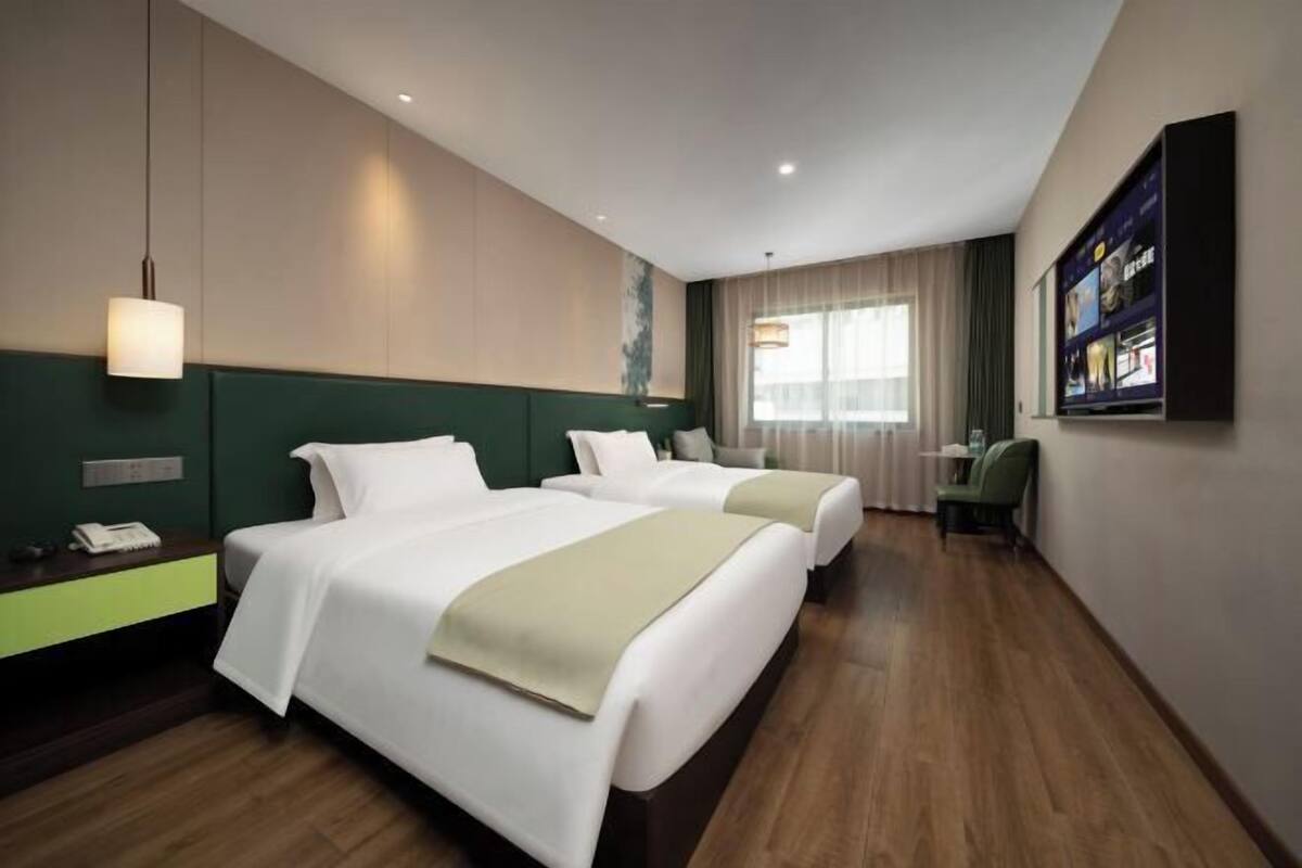 Quarto de hotel com duas camas, uma escrivaninha, uma cadeira, uma televisão e uma janela com cortinas.