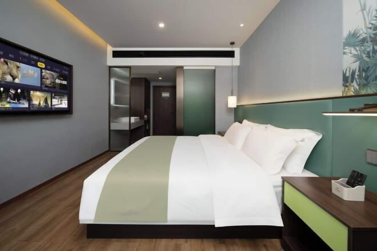 Quarto de hotel moderno com uma cama grande, televisão presa à parede e uma parede de destaque verde.