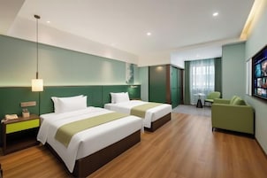 Quarto de hotel com duas camas, um sofá verde, uma mesa pequena e vista para o exterior.