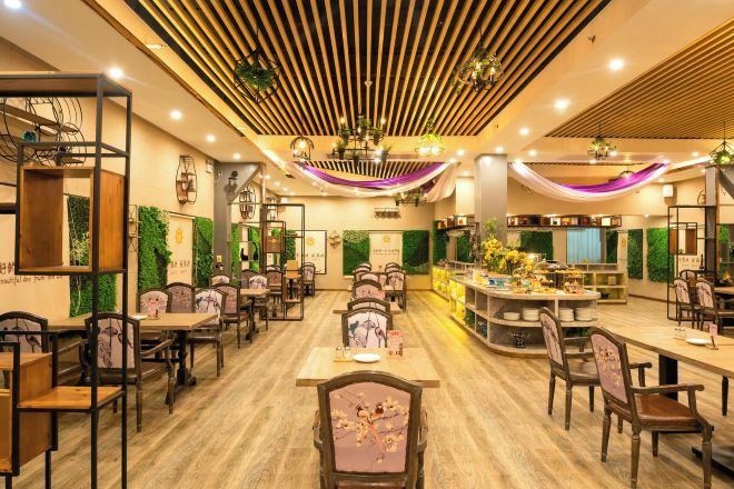 Restaurante com várias mesas e cadeiras, teto de madeira e plantas decorativas.