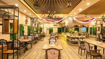 Restaurante com várias mesas e cadeiras, teto de madeira e plantas decorativas.