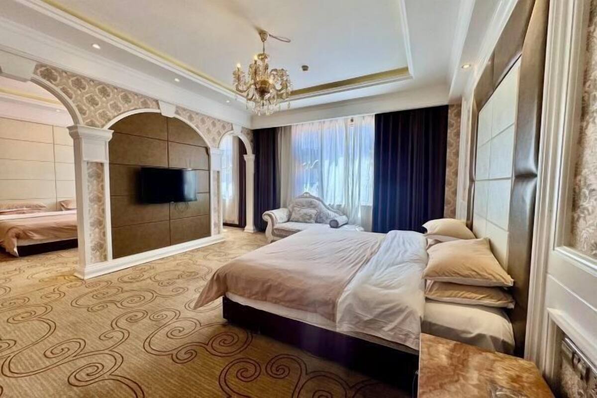 Um quarto espaçoso com uma cama grande, uma televisão fixada na parede e um lustre.