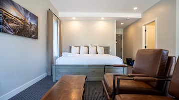 Quarto de hotel moderno com uma cama grande, um banco de madeira e uma poltrona de couro marrom.