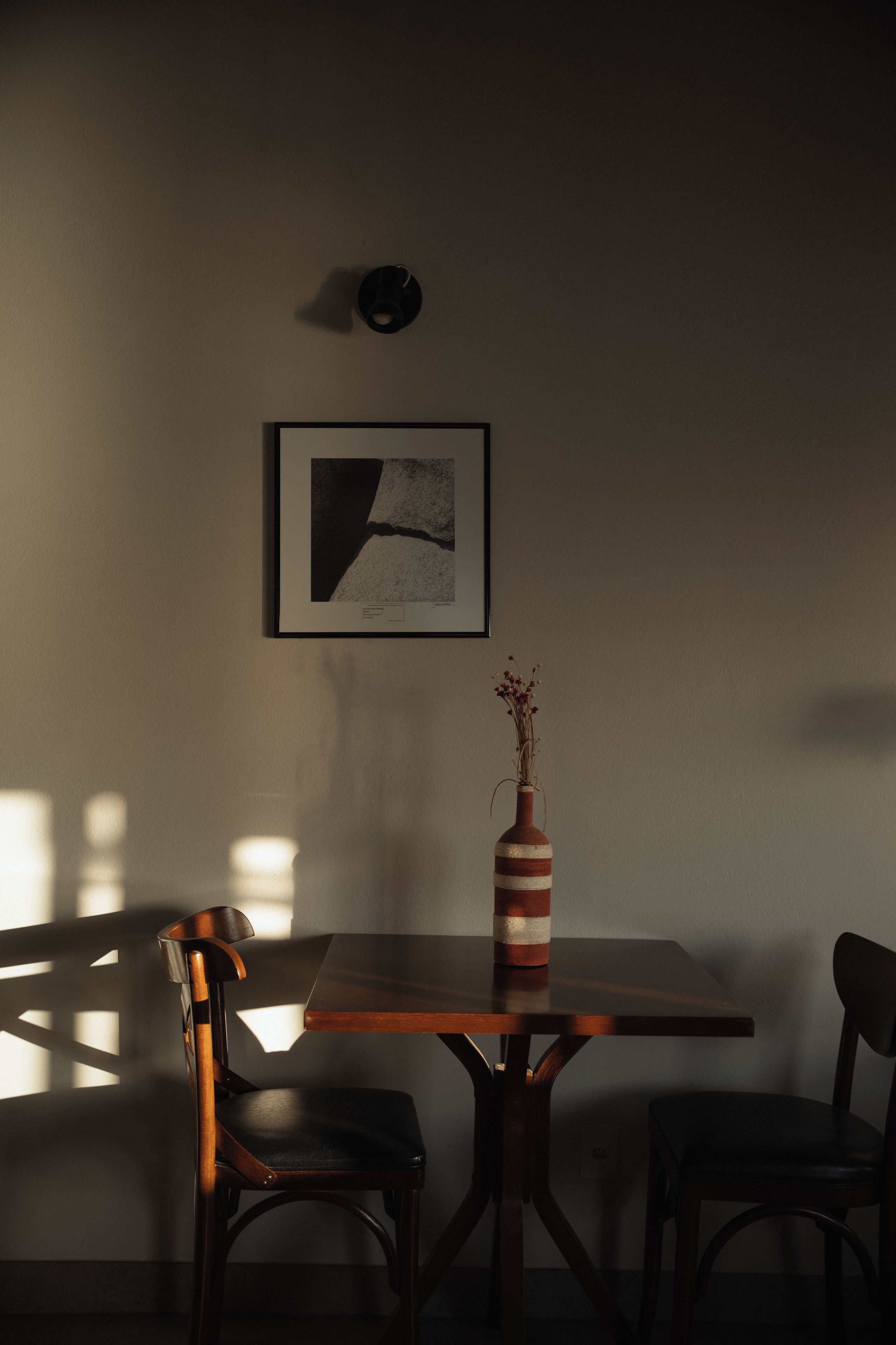 Uma sala de jantar com uma mesa, cadeiras, um vaso com flores e um quadro na parede.