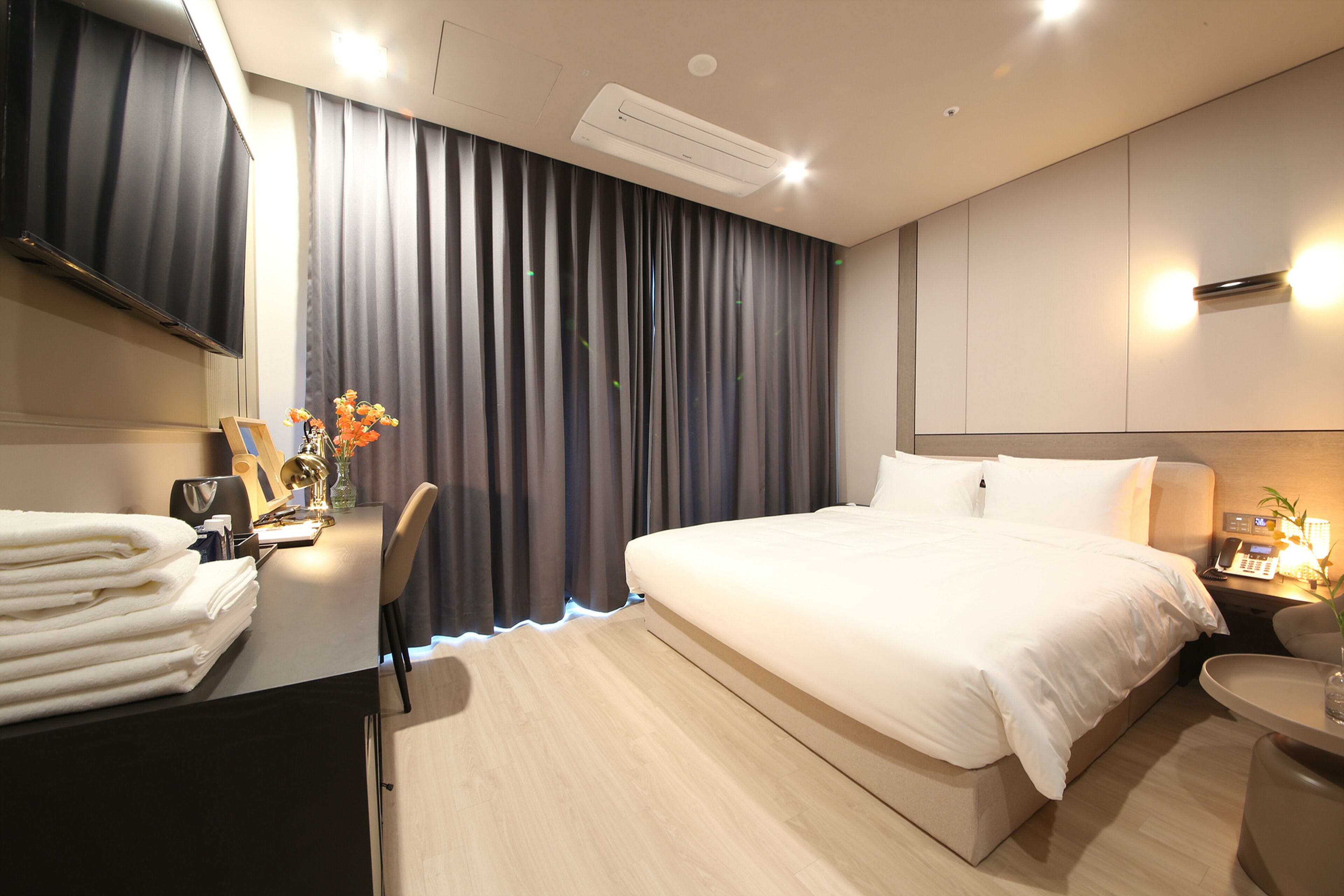 Quarto de hotel moderno com uma cama grande, uma escrivaninha com cadeira, uma mesinha e um espelho.