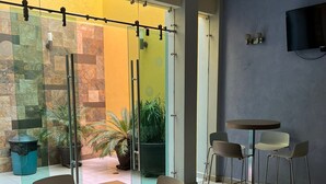 Um espaço interior moderno com uma mesa e cadeiras de madeira, uma porta de vidro que dá para o exterior, e uma televisão fixada na parede.