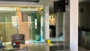 Um lobby moderno com sofás de couro, uma mesa de centro de vidro e uma TV de tela plana fixada na parede.