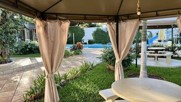 Uma área de estar coberta ao ar livre, com piscina ao fundo.