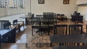 Uma sala de jantar com mesas, cadeiras, uma televisão e duas fotografias emolduradas na parede.