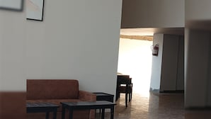 Um corredor com um sofá marrom, duas mesas pretas e uma cadeira.