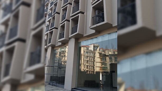 Um edifício moderno com fachada geométrica, várias varandas e grandes janelas de vidro que refletem o ambiente.
