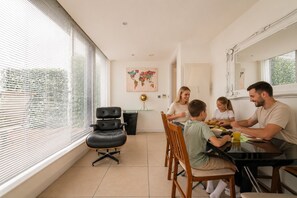 Uma família jantando em um espaço com uma grande janela, um mapa na parede e uma cadeira de escritório preta.