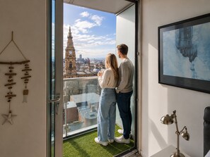 Um casal em uma varanda com vista para a paisagem urbana, incluindo um campanário.
