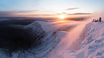 Paisagem montanhosa coberta de neve com nascer ou pôr do sol, mostrando um grupo de pessoas em um cume.