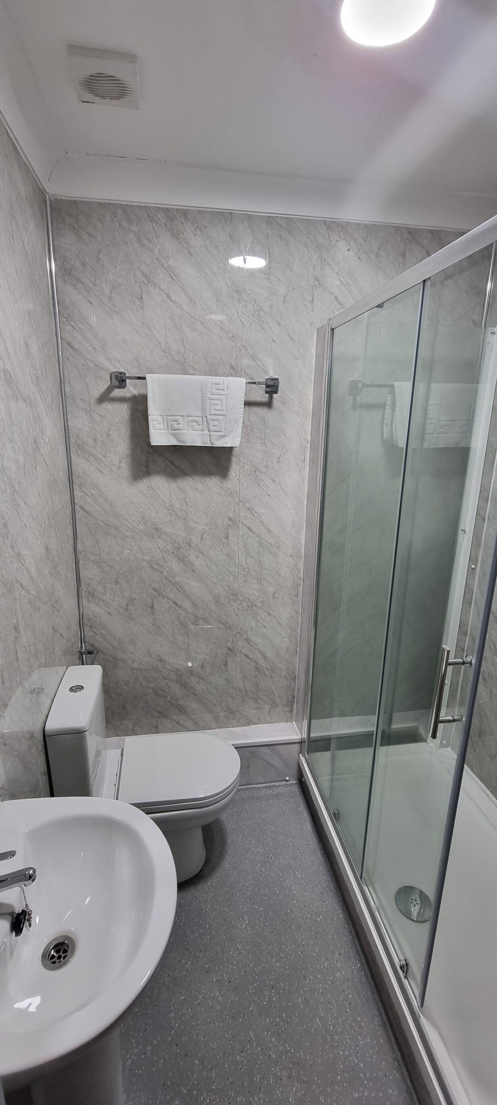 Uma casa de banho compacta com cabine de duche em vidro, sanita e lavatório.