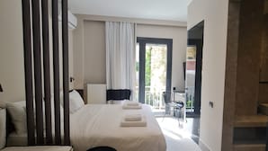 Quarto de hotel moderno com uma cama grande, uma mesa redonda pequena, uma cadeira e vista para a varanda.