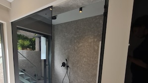 Uma casa de banho moderna com cabine de duche em vidro, lavatório embutido e parede de mármore.