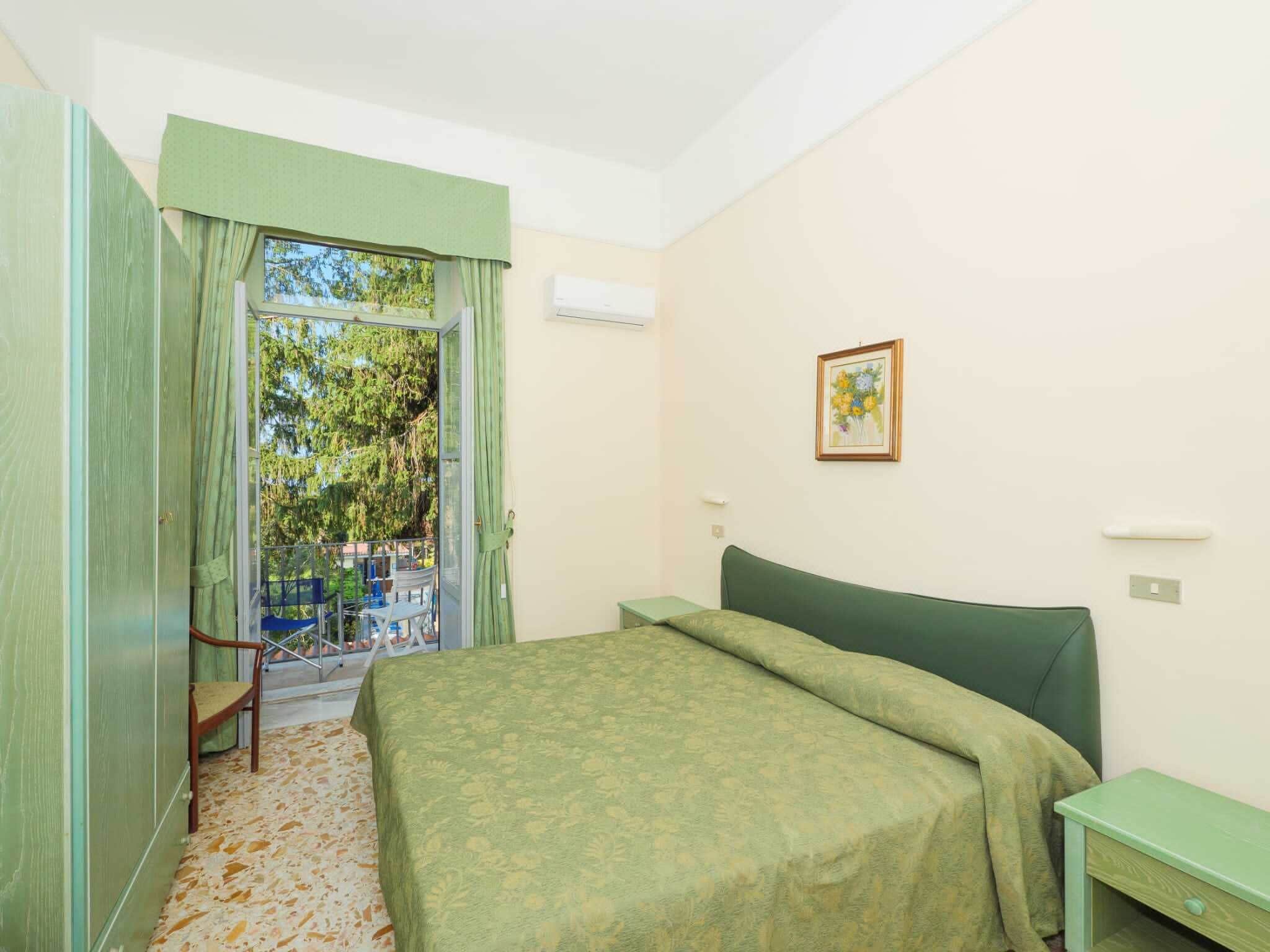 Quarto com cama, mesa de cabeceira, cadeira e janela com cortinas.