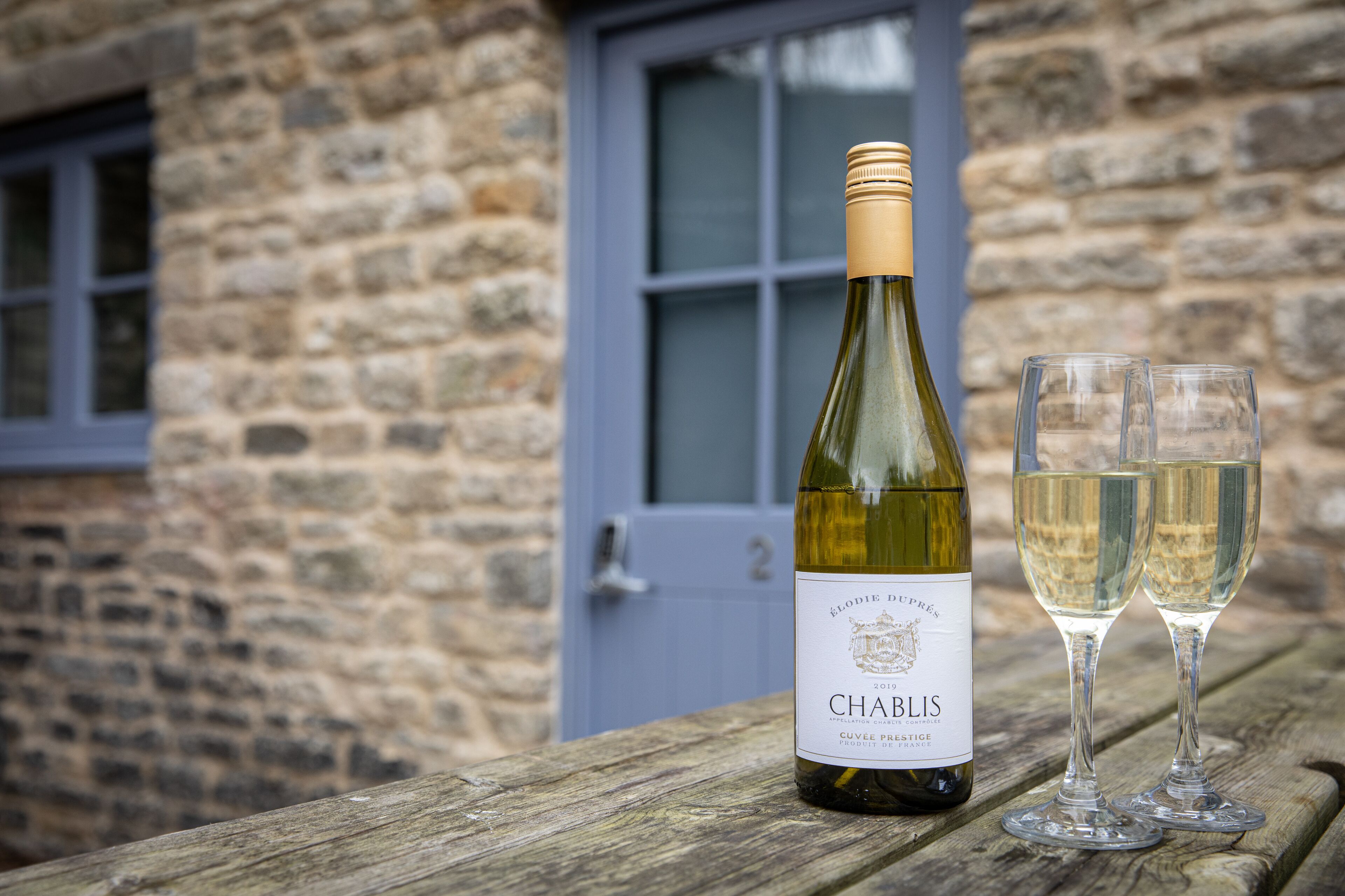 Uma garrafa de vinho Chablis e duas taças sobre uma mesa de madeira.