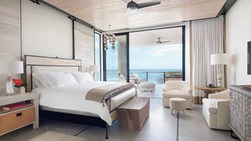 Quarto moderno com uma cama grande, ventilador de teto, vista para o oceano e varanda com assentos.
