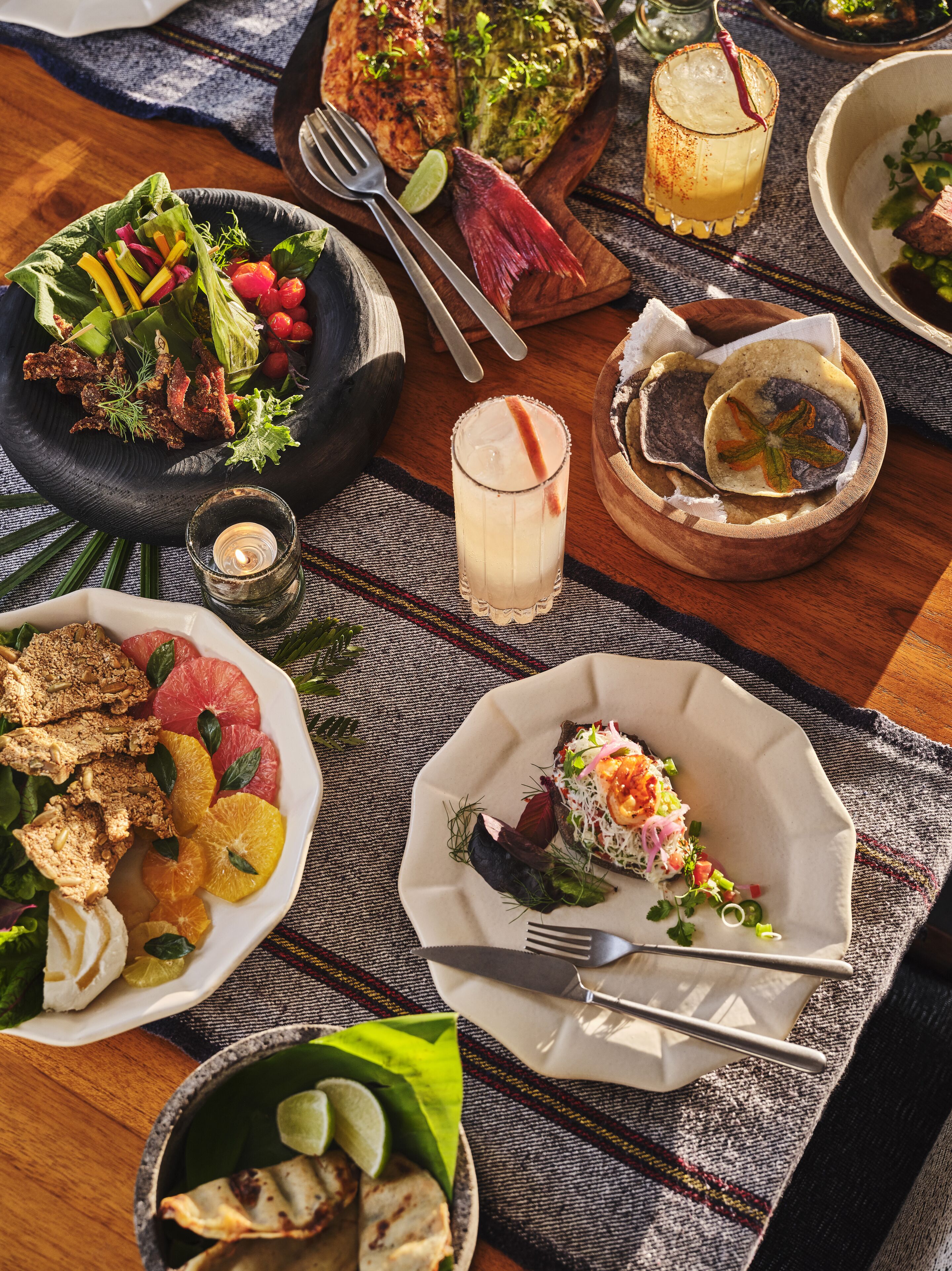 Mesa posta com diversos pratos, incluindo uma salada, carne grelhada e uma bebida.