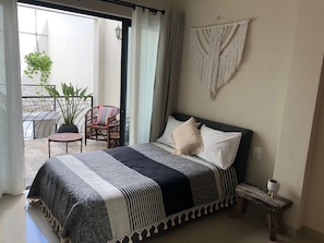 Um quarto com uma cama, um painel de macramé, uma cadeira e um vaso com planta.