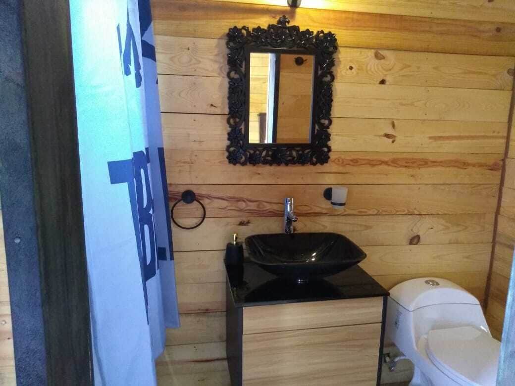 Casa de banho compacta com parede de madeira, lavatório preto, sanita branca e espelho decorativo.
