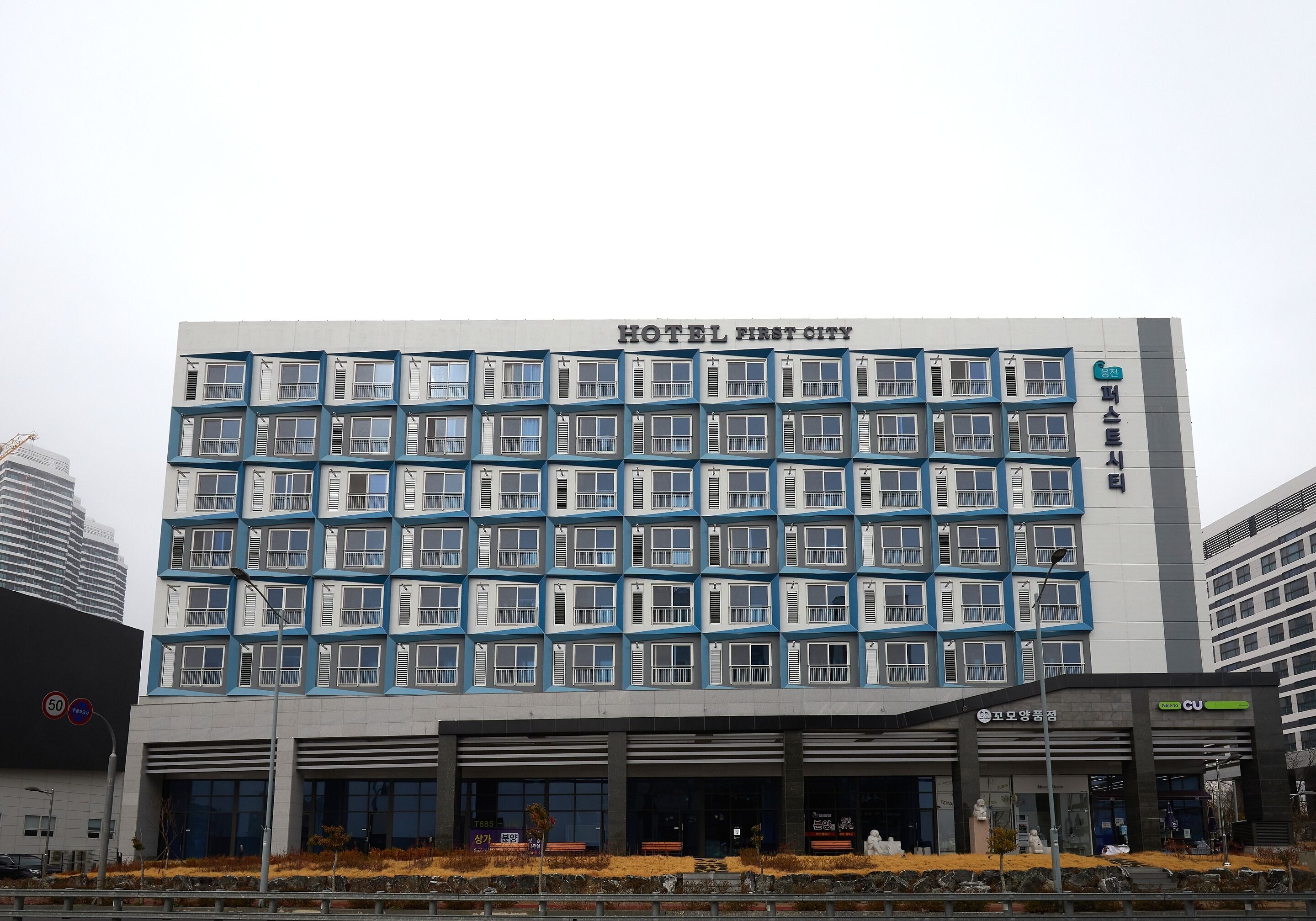 Um hotel de vários andares com fachada moderna, destacando uma grade de janelas e uma sinalização chamativa com a inscrição "HOTEL FIRST CITY".