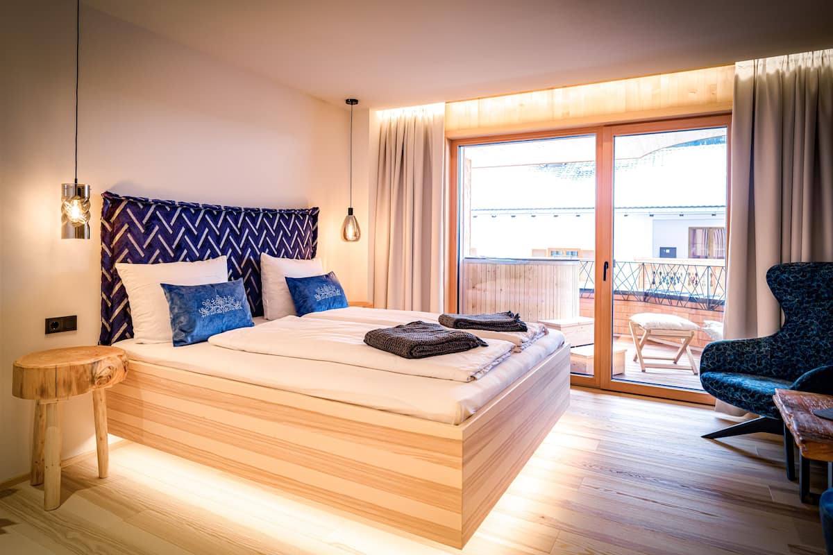 Quarto moderno com cama grande, piso de madeira, vista para a varanda e cabeceira estampada em azul.