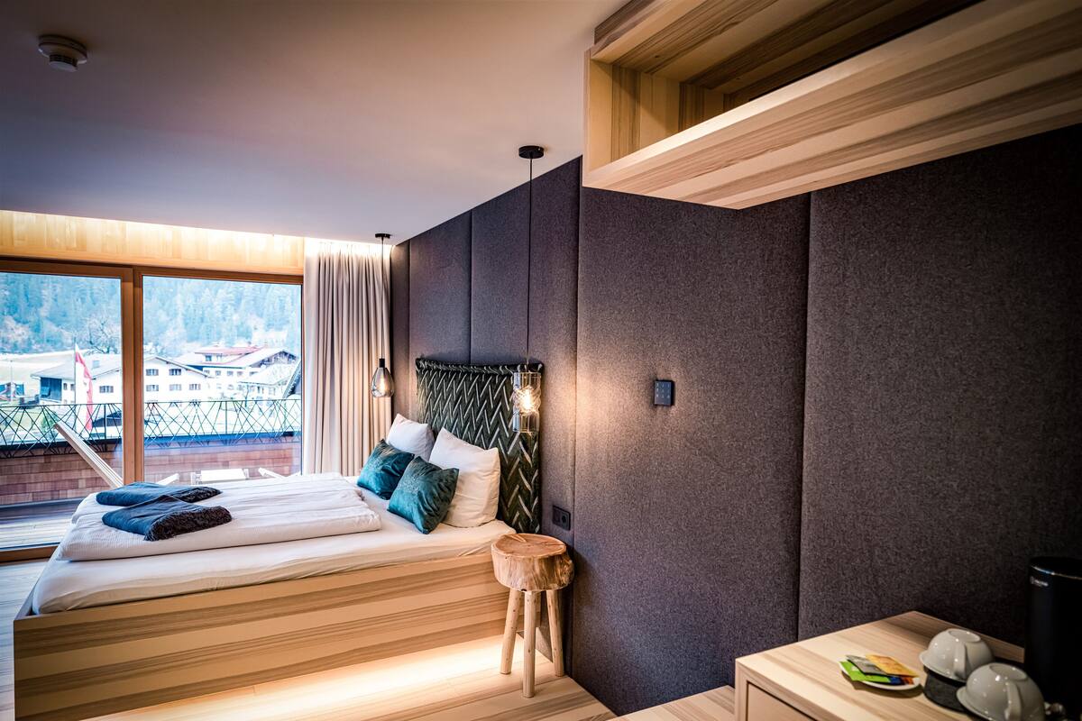 Quarto moderno com uma cama grande, uma mesa de cabeceira pequena e vista para o exterior.