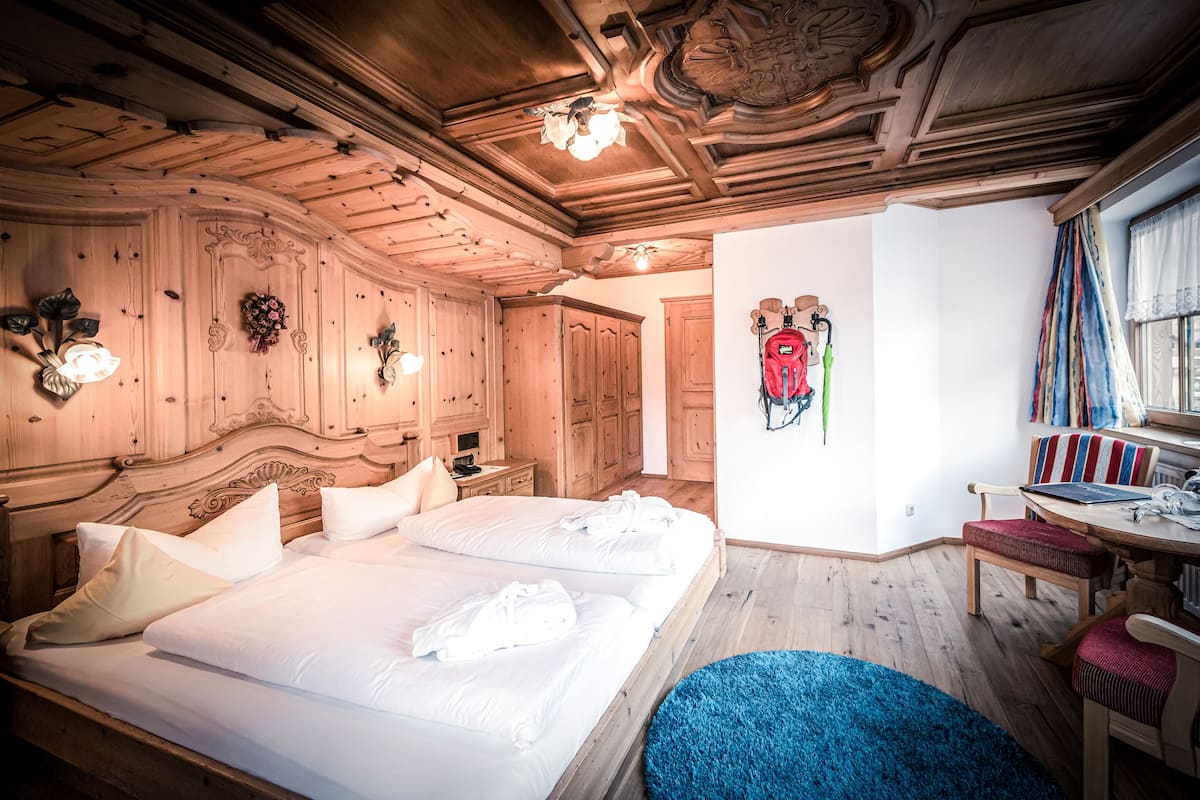 Quarto com painéis de madeira, uma cama grande, uma mesinha e uma cadeira.