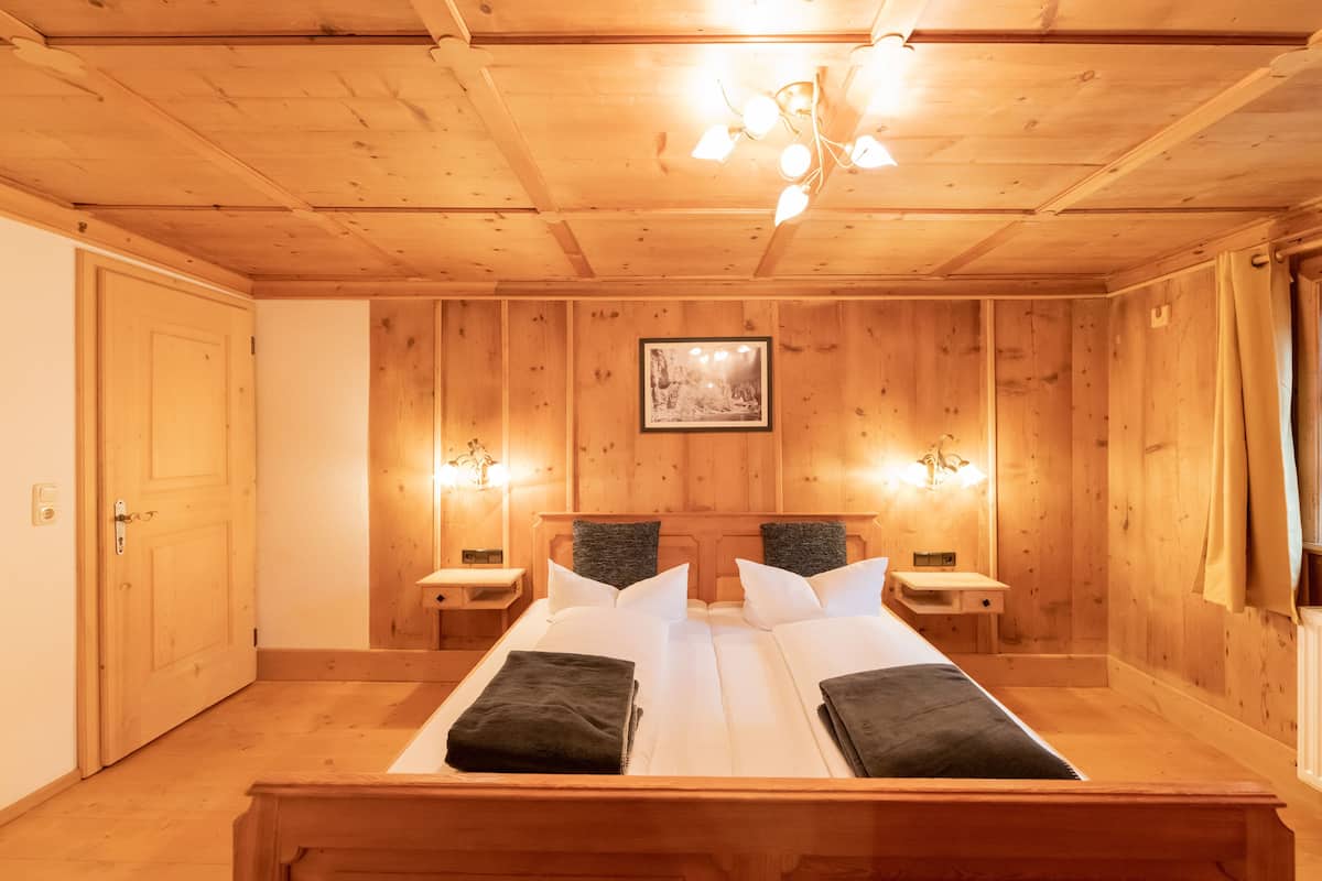 Um quarto com painéis de madeira, uma cama, duas mesas de cabeceira e um lustre.
