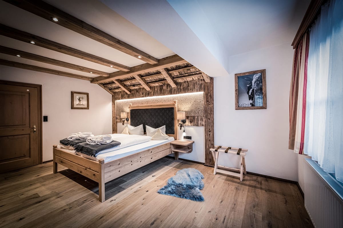 Quarto com cama de madeira, mesa de cabeceira, mesinha, tapete de pele e um quadro na parede.