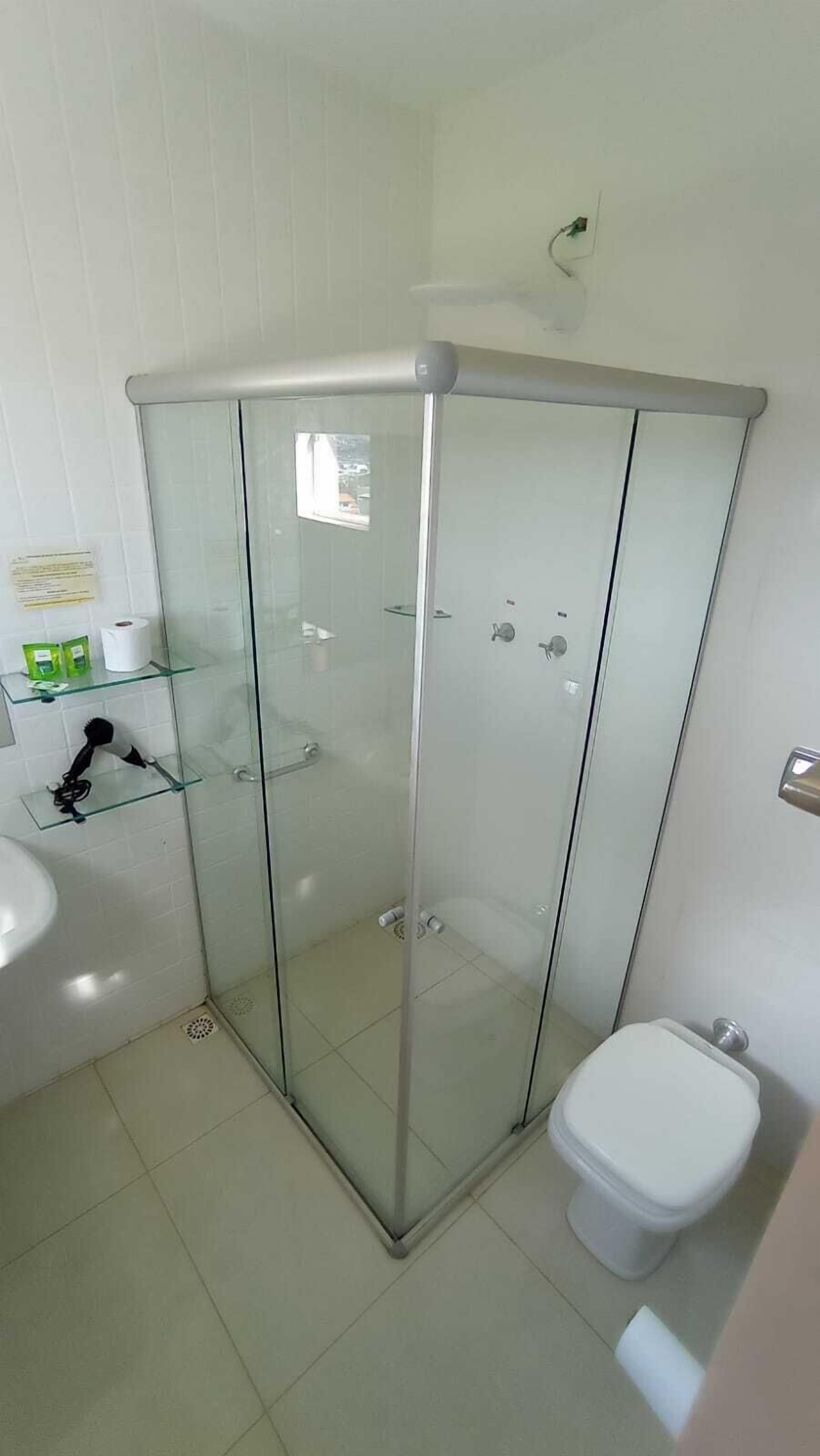 Casa de banho com cabine de duche em vidro, sanita e lavatório com produtos de higiene.
