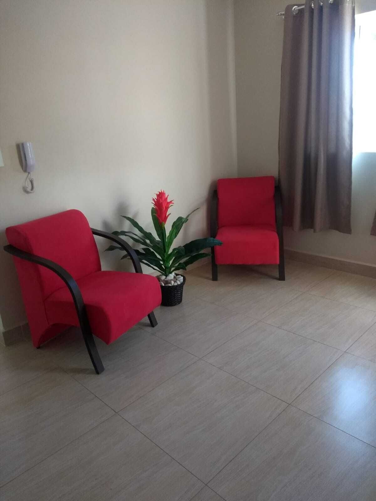 Quarto com duas cadeiras vermelhas, um vaso de planta e um telefone na parede.