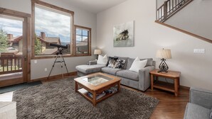 Uma sala de estar com um sofá cinzento, uma mesa de centro de vidro, uma mesinha de cabeceira de madeira e um quadro de um lobo na parede.