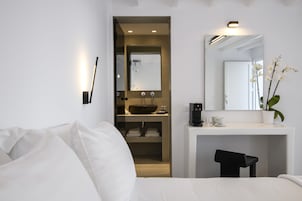 Quarto de hotel moderno com uma cama grande, uma pequena escrivaninha com pia, um espelho e uma orquídea em vaso.
