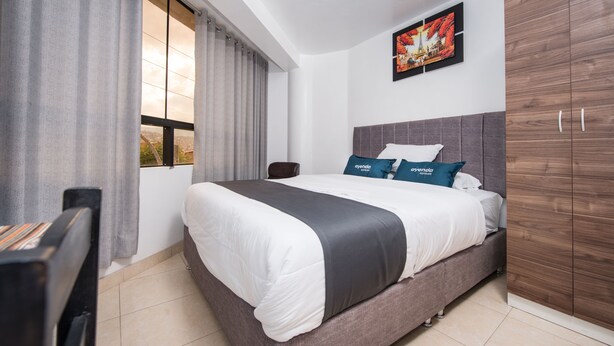 Quarto com uma cama grande, uma escrivaninha, uma cadeira, um guarda-roupa e uma janela com cortinas.