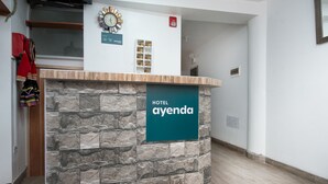 Uma área de recepção com parede de pedra, um relógio e uma placa que diz 'HOTEL ayenda'.