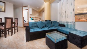 Uma sala de estar com sofá seccional, uma mesa de centro de vidro e um espaço de refeições com cadeiras e mesa.