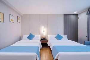 Quarto de hotel com duas camas, uma mesinha de cabeceira e uma luminária fixada na parede.