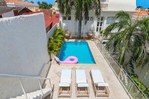Piscina com espreguiçadeiras, boia rosa e palmeiras.