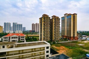 Vista de edifícios residenciais altos, com vários andares e varandas, em meio ao verde e sob um céu claro.