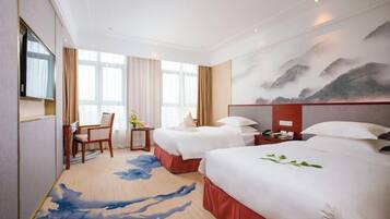 Quarto de hotel com duas camas, uma escrivaninha, uma cadeira e um quadro grande na parede.