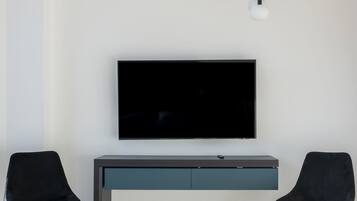 Quarto moderno com televisão de tela plana presa a um armário azul escuro, duas cadeiras pretas e um pendente simples.