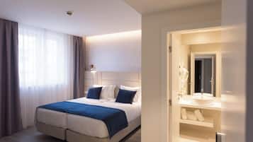 Quarto de hotel moderno com uma cama grande, uma mesinha de cabeceira e um banheiro visível por uma porta aberta.