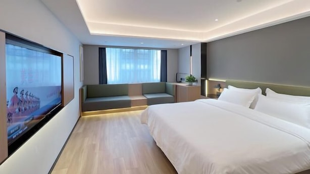 Quarto de hotel moderno com uma cama grande, área de estar, televisão de tela plana e uma janela ampla.