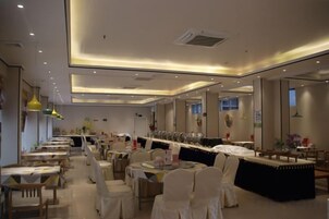 Uma sala de jantar ampla, com várias mesas e cadeiras, um balcão comprido e iluminação pendente.
